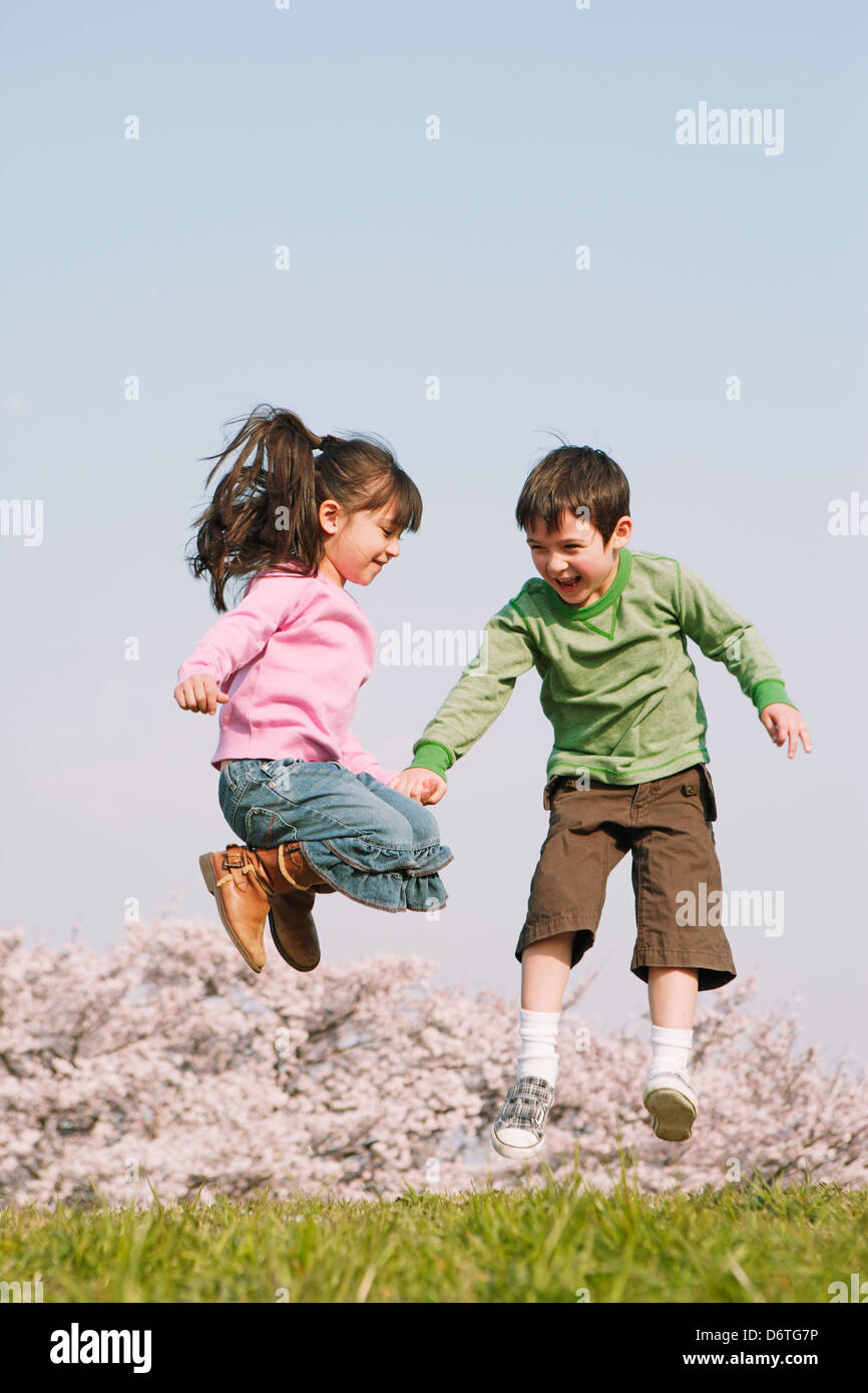 Children holding hands jumping on grassland Stock Photo - Alamy