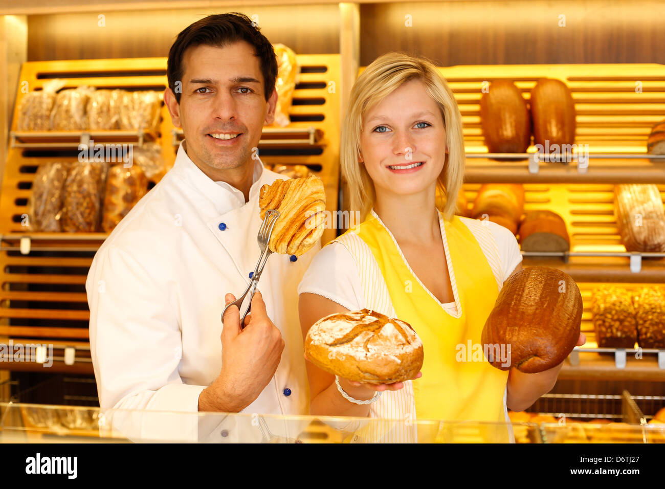 Bakery shopkeeper and baker present different types of pastry in shop ...