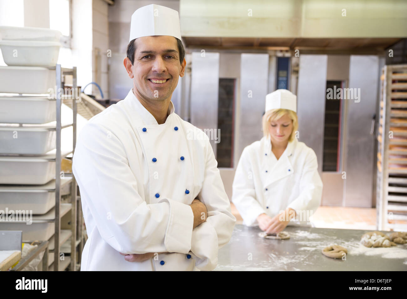 Baker posing in bakery or bakehouse. Another baker is working in the ...