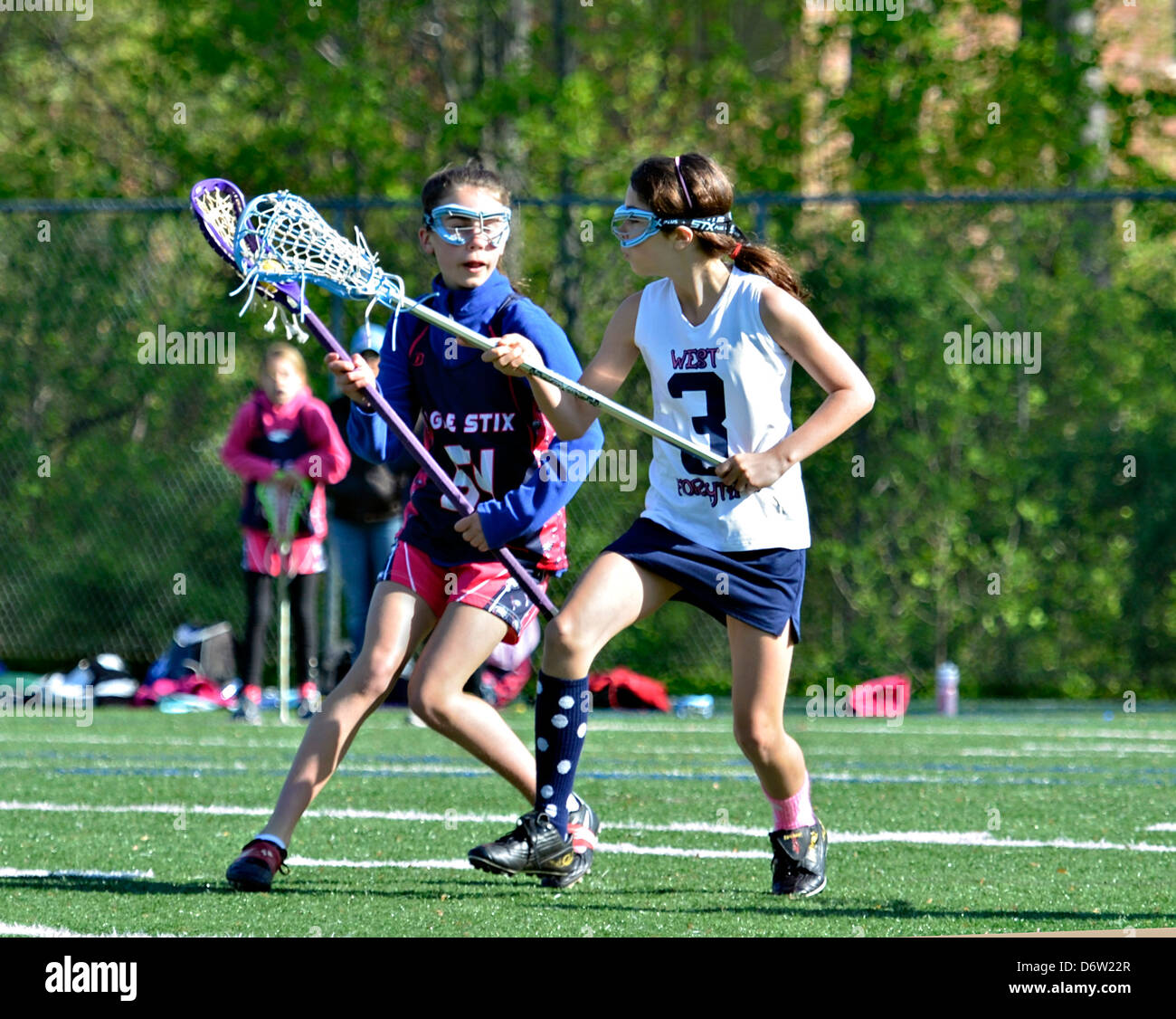 Two young girls making a play during a lacrosse game, one passing one ...