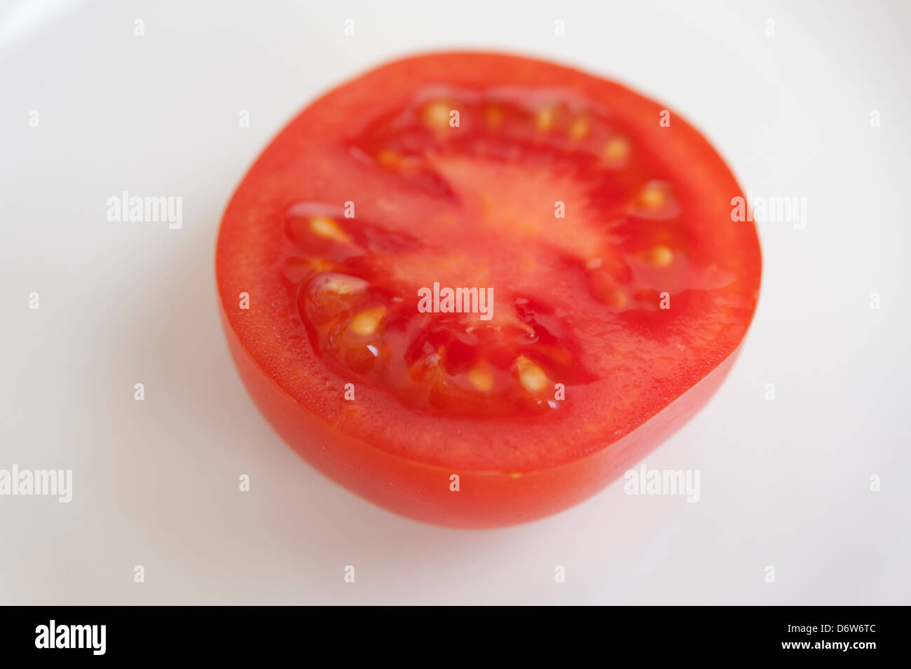 A tomato sliced in half on a white plain background Stock Photo - Alamy