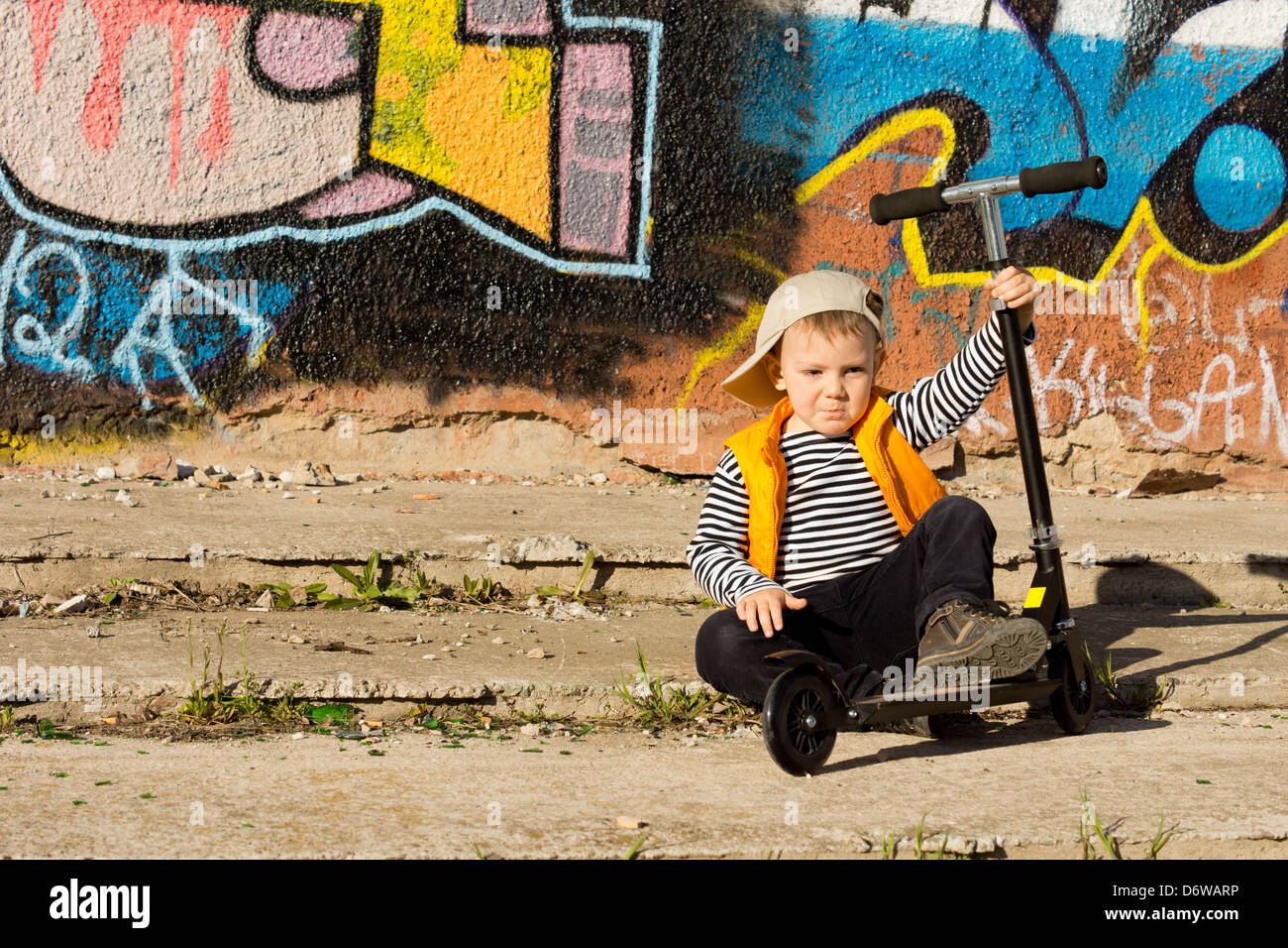 Adorable young boy sitting on the ground with his scooter held upright ...