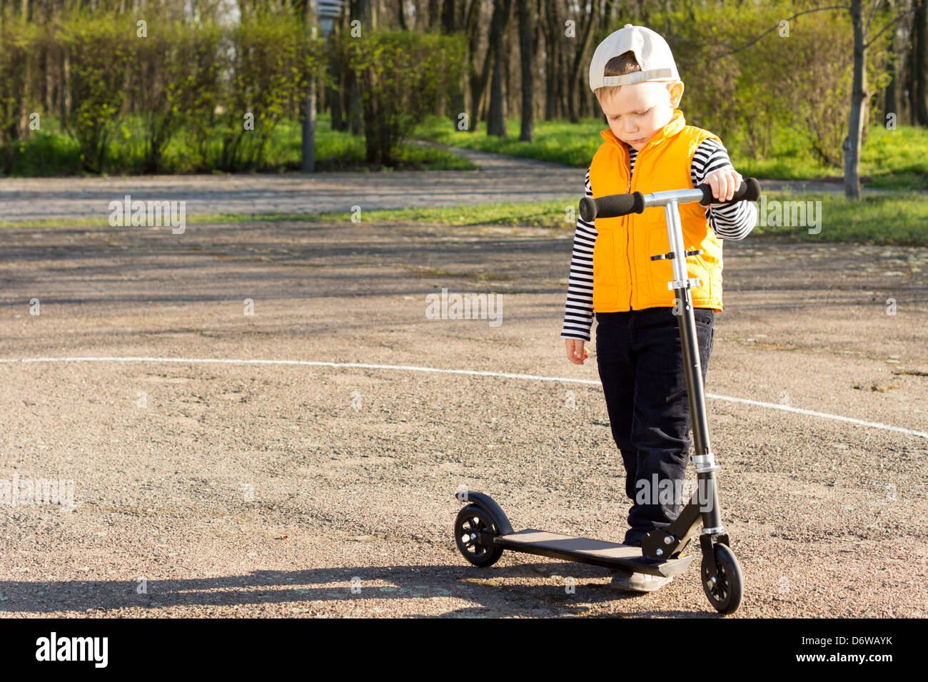Handsome little boy with his scooter standing on a tarred country lane ...