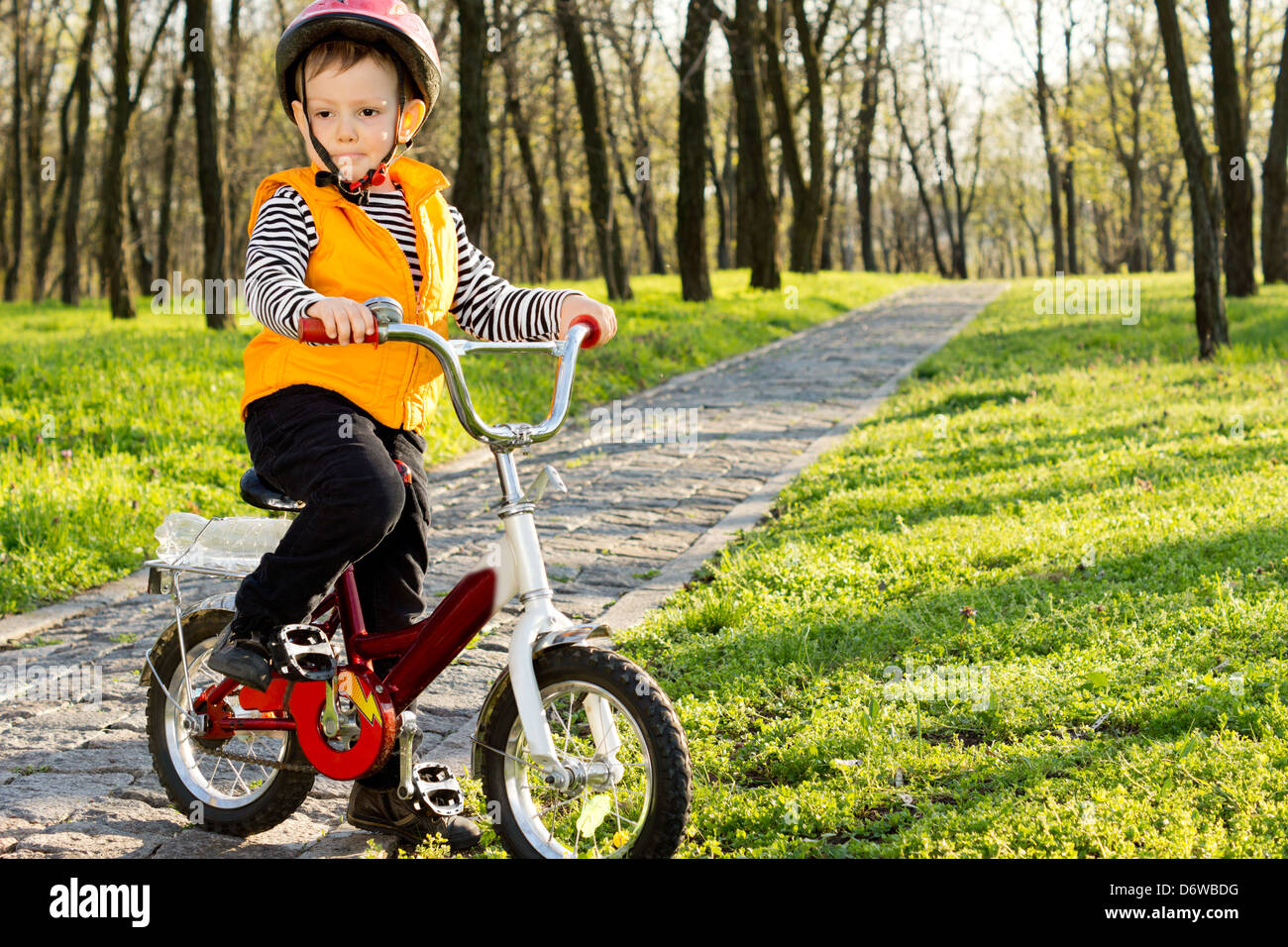 Adorable little boy riding his bike along a paved path in a wooded park ...