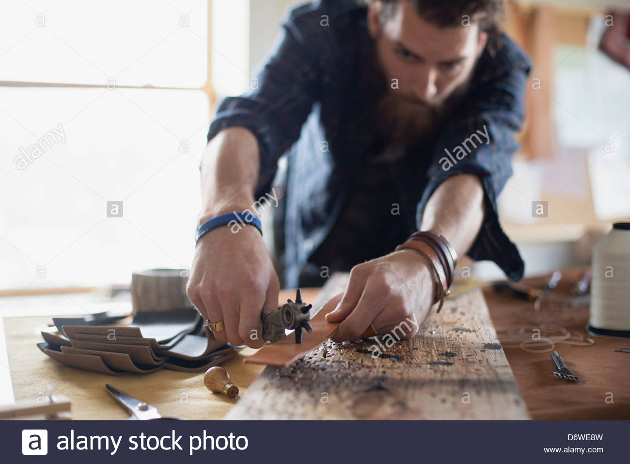 Man punching holes in leather belt at table Stock Photo - Alamy