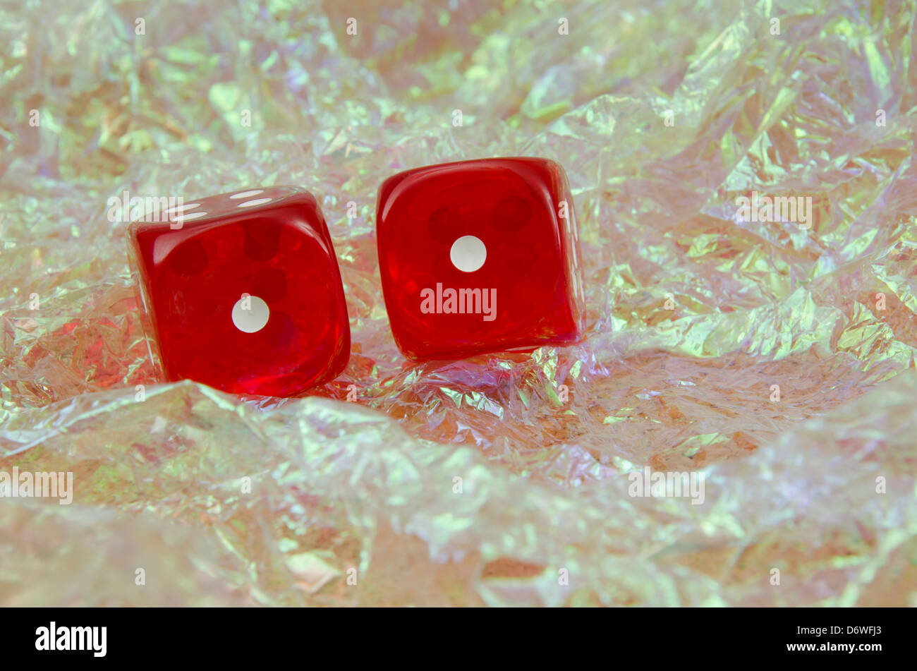 Pair of red dice over a bright, pearly bakground showing two ones ...