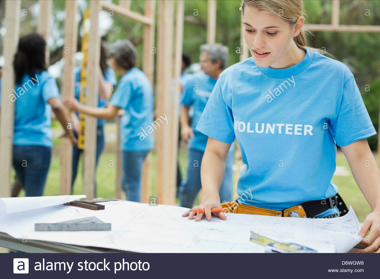 Beautiful young woman looking at blueprint with volunteers working in ...