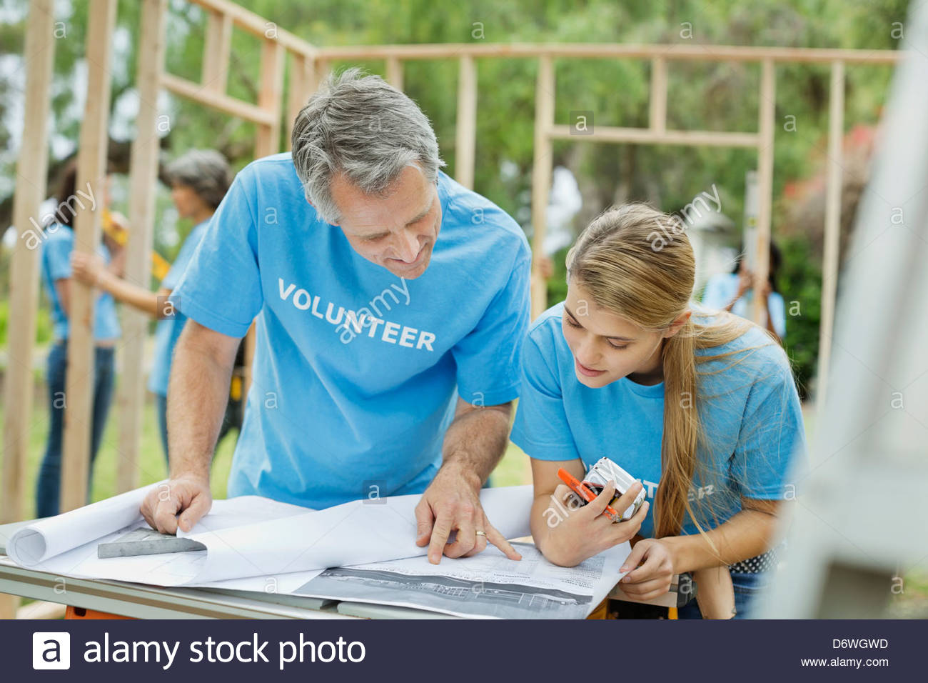 Two volunteers discussing blueprint while people work in background ...