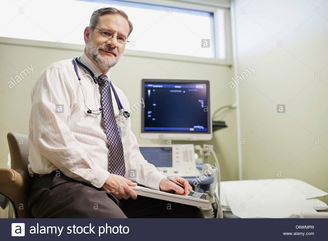Portrait of male doctor with clipboard sitting in examination room ...