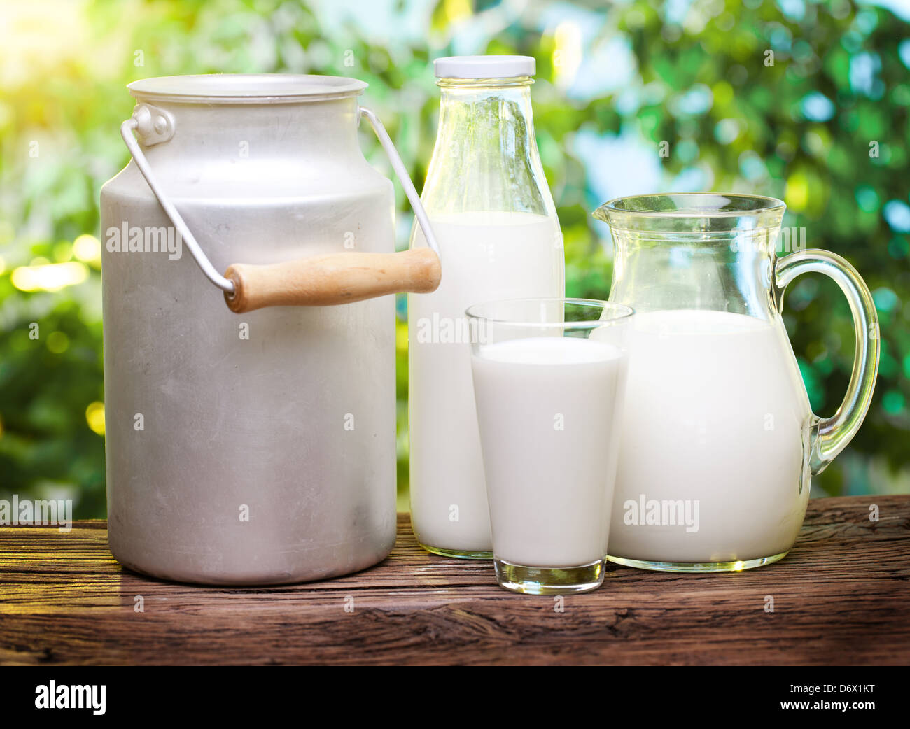 Milk in various dishes on the old wooden table in an outdoor setting ...