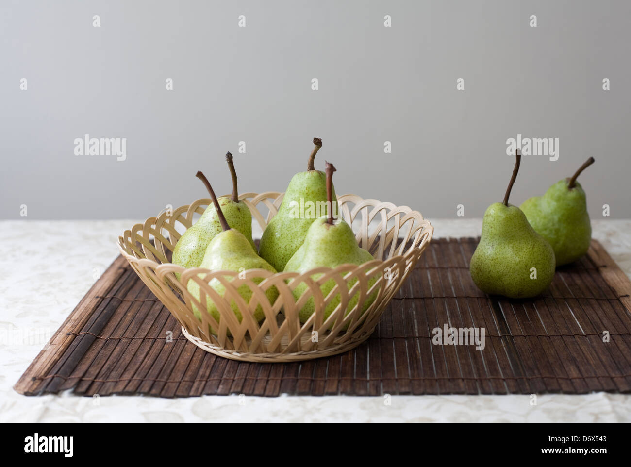 Six green pears in a woven rattan dish and on a bamboo mat with a light ...