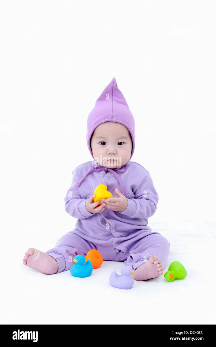 baby in purple clothes and hat playing with colourful duck toys Stock ...