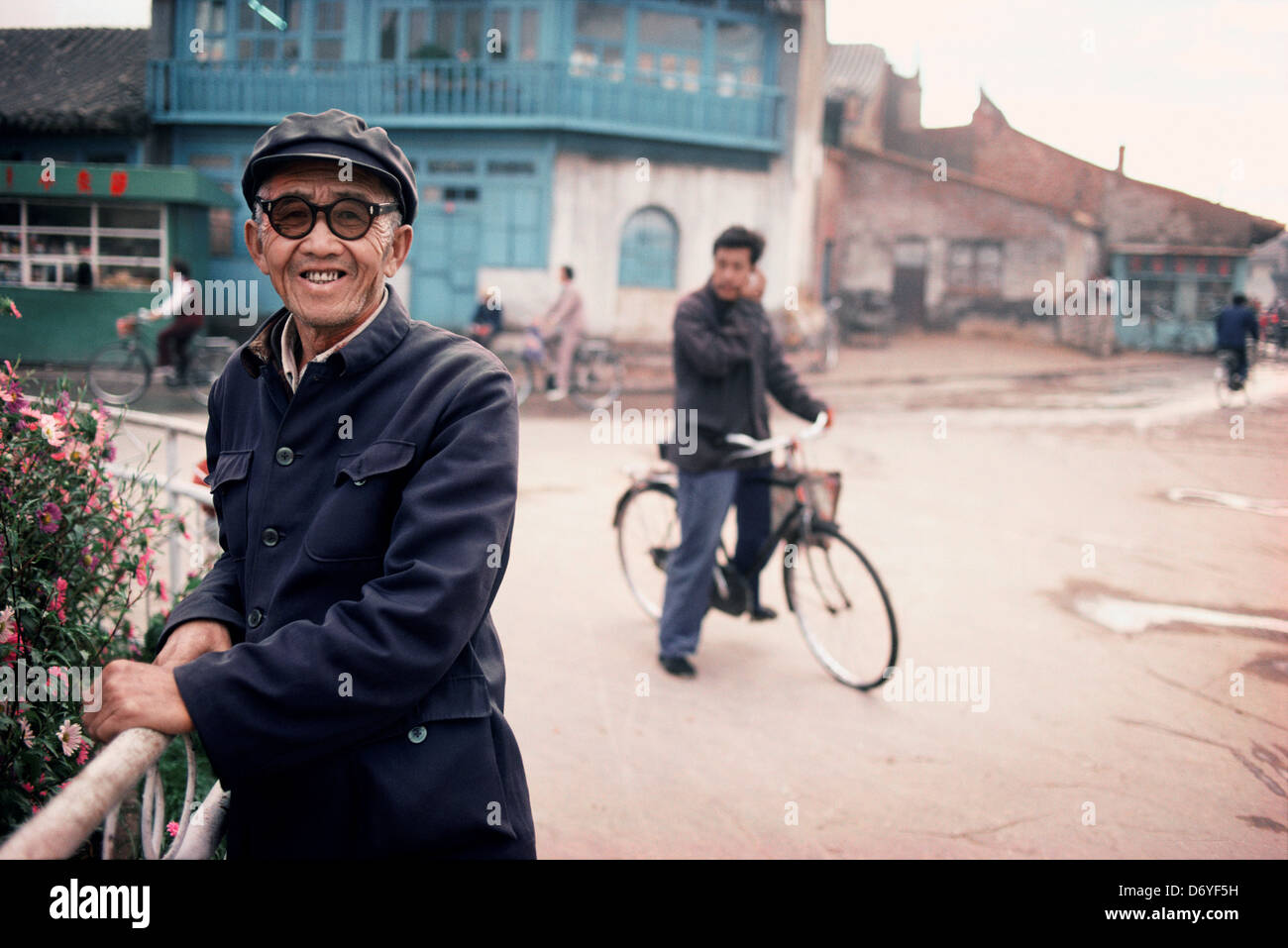 Man leaning against a railing with another man riding bicycle in the ...