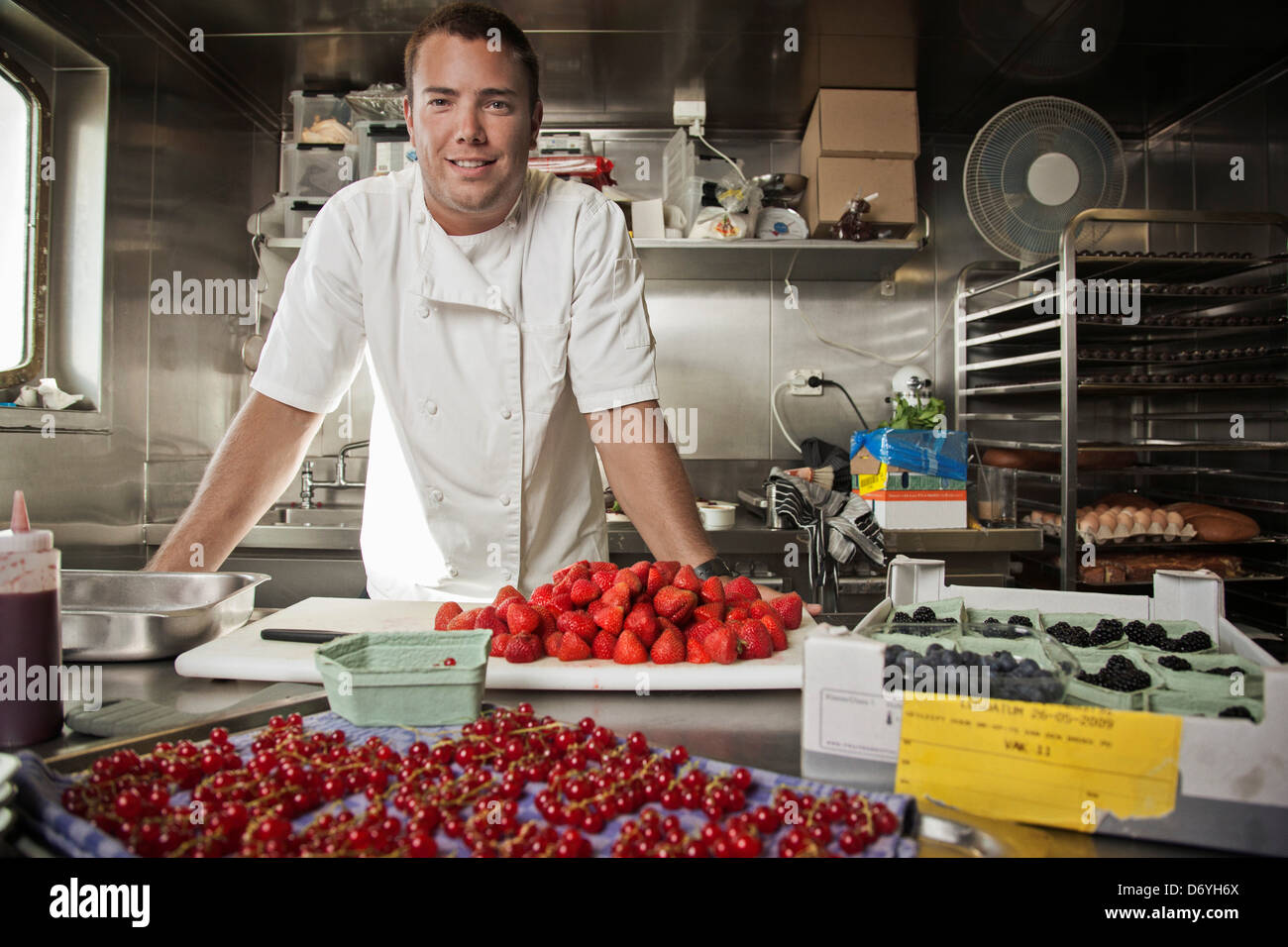 Pastry chef leaning on counter in kitchen. Strawberries, blueberries ...