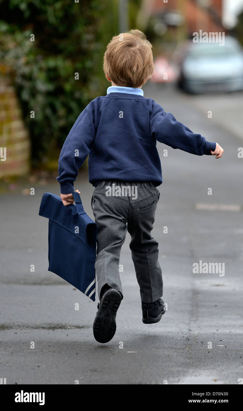 A five year old boy wearing his school uniform running along a pavement ...
