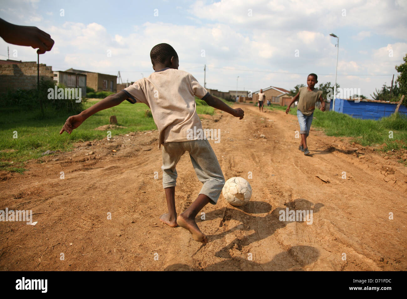 African boys play soccer in the dirt road in a small rural settlement ...