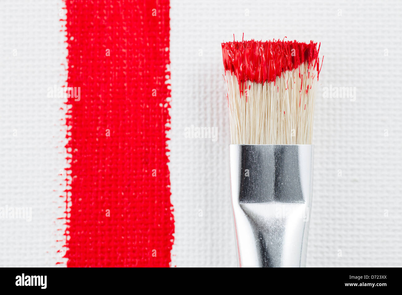 Paint brush with red paint on the end beside red paint stroke on cavas ...