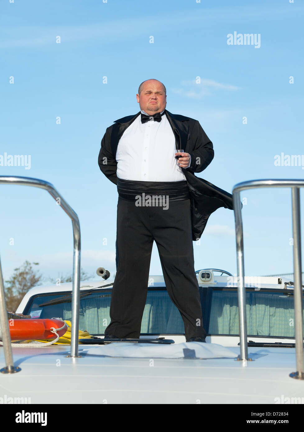 Overweight man in tuxedo standing on the deck of a luxury pleasure boat ...