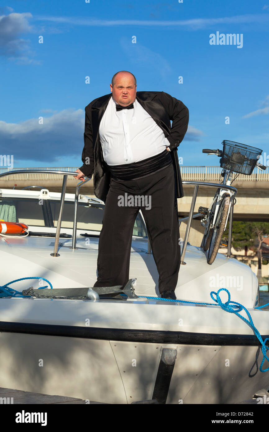 Overweight man in tuxedo standing on the deck of a luxury pleasure boat ...