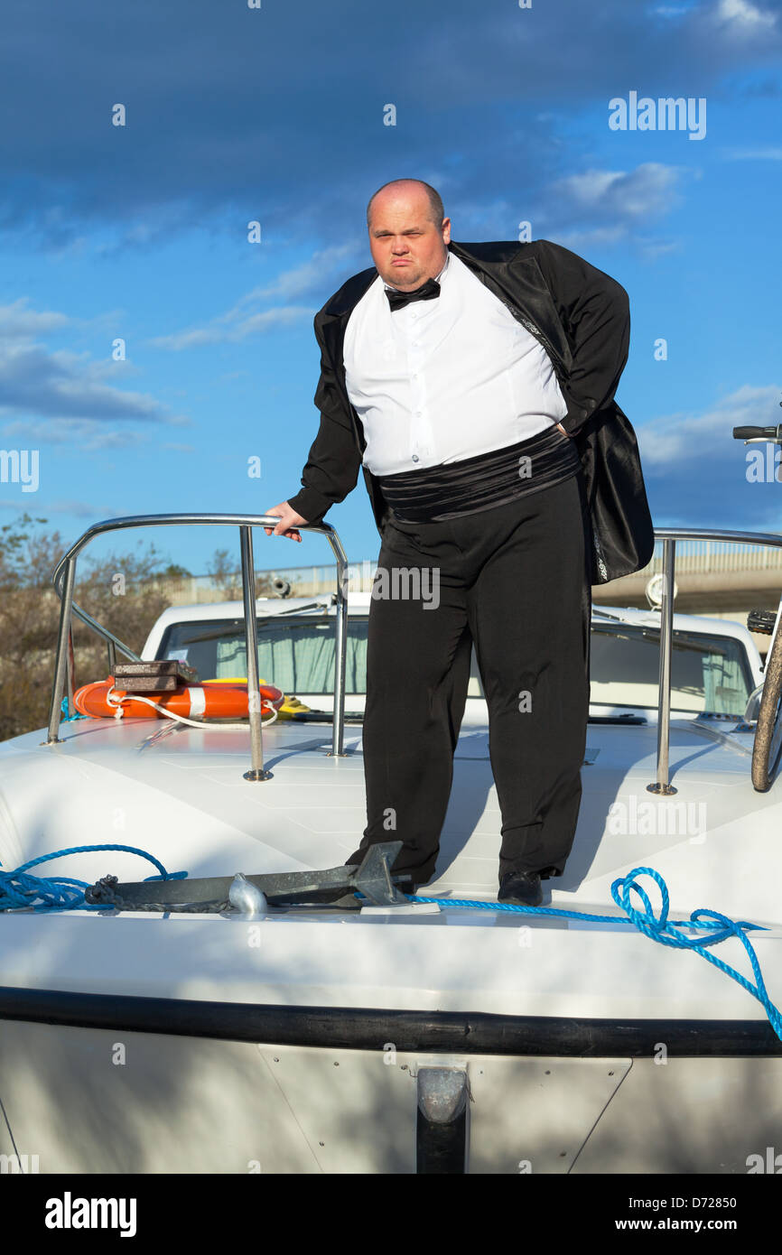 Overweight man in tuxedo standing on the deck of a luxury pleasure boat ...