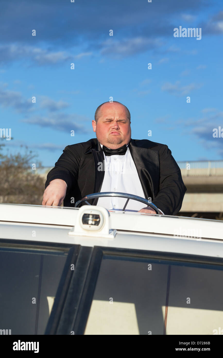 Overweight man in a tuxedo at the helm of a pleasure boat, closeup ...