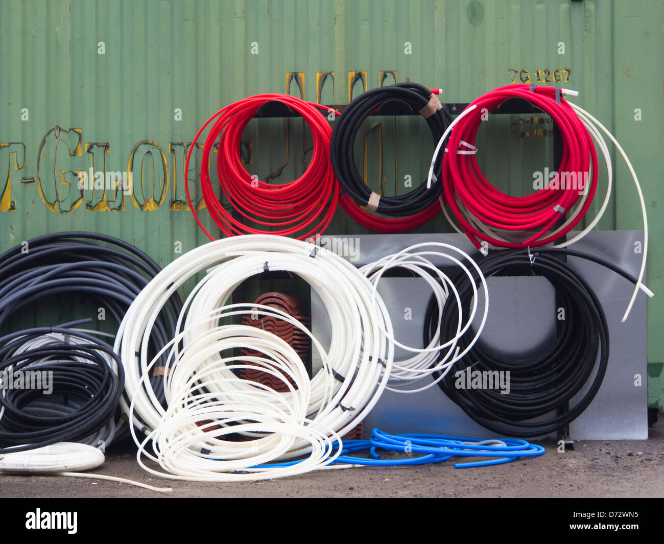 Red black blue and white coils of plastic pipes set up against a green ...