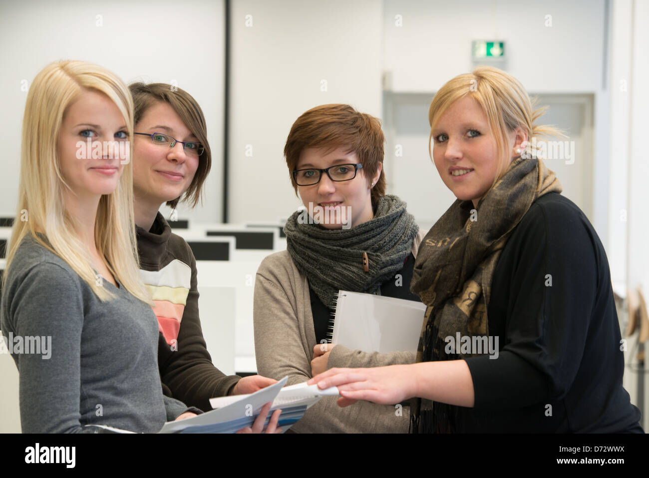 four female students standing in university auditorium and discussing ...