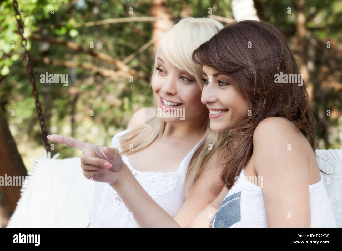 Two beautiful female friends resting on swing and talking. Selective ...