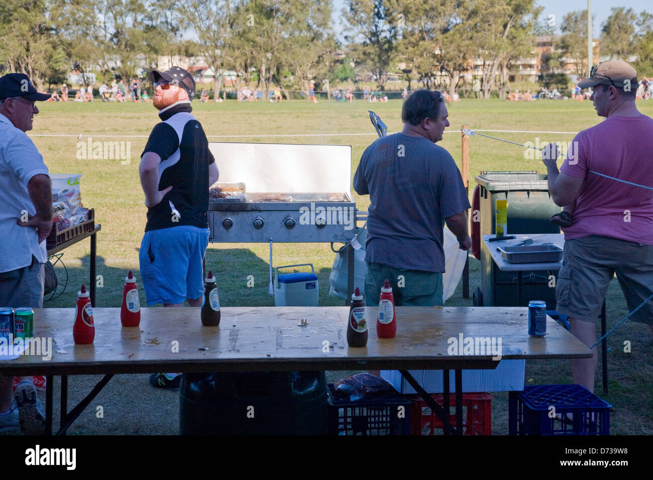 men cooking at a barbeque whilst watching australian rugby league game ...
