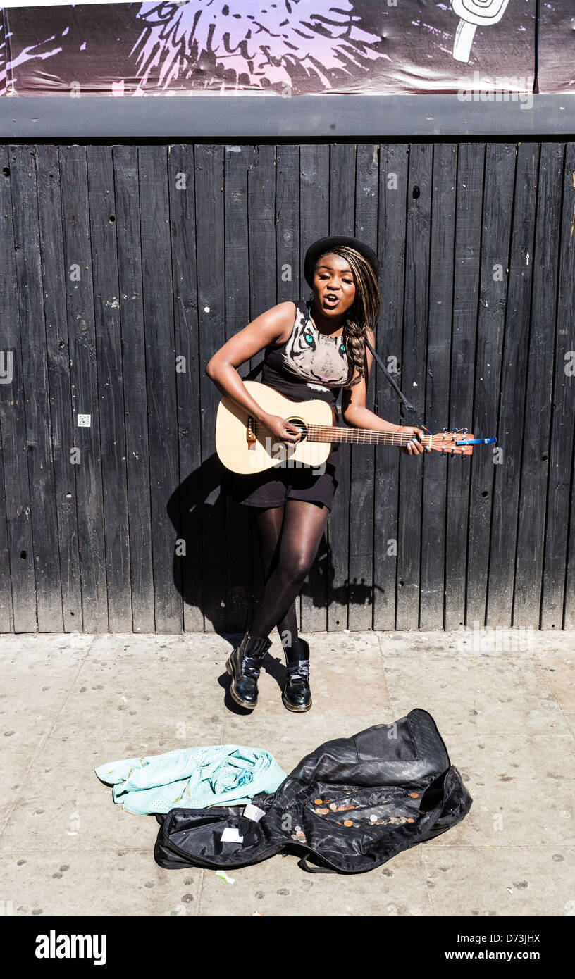 Portrait of a trendy, young, black female busker playing guitar and ...