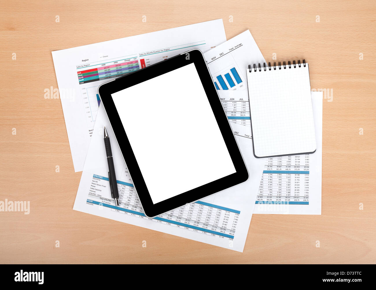 Tablet and notepad over papers with numbers and charts, coffee cup ...