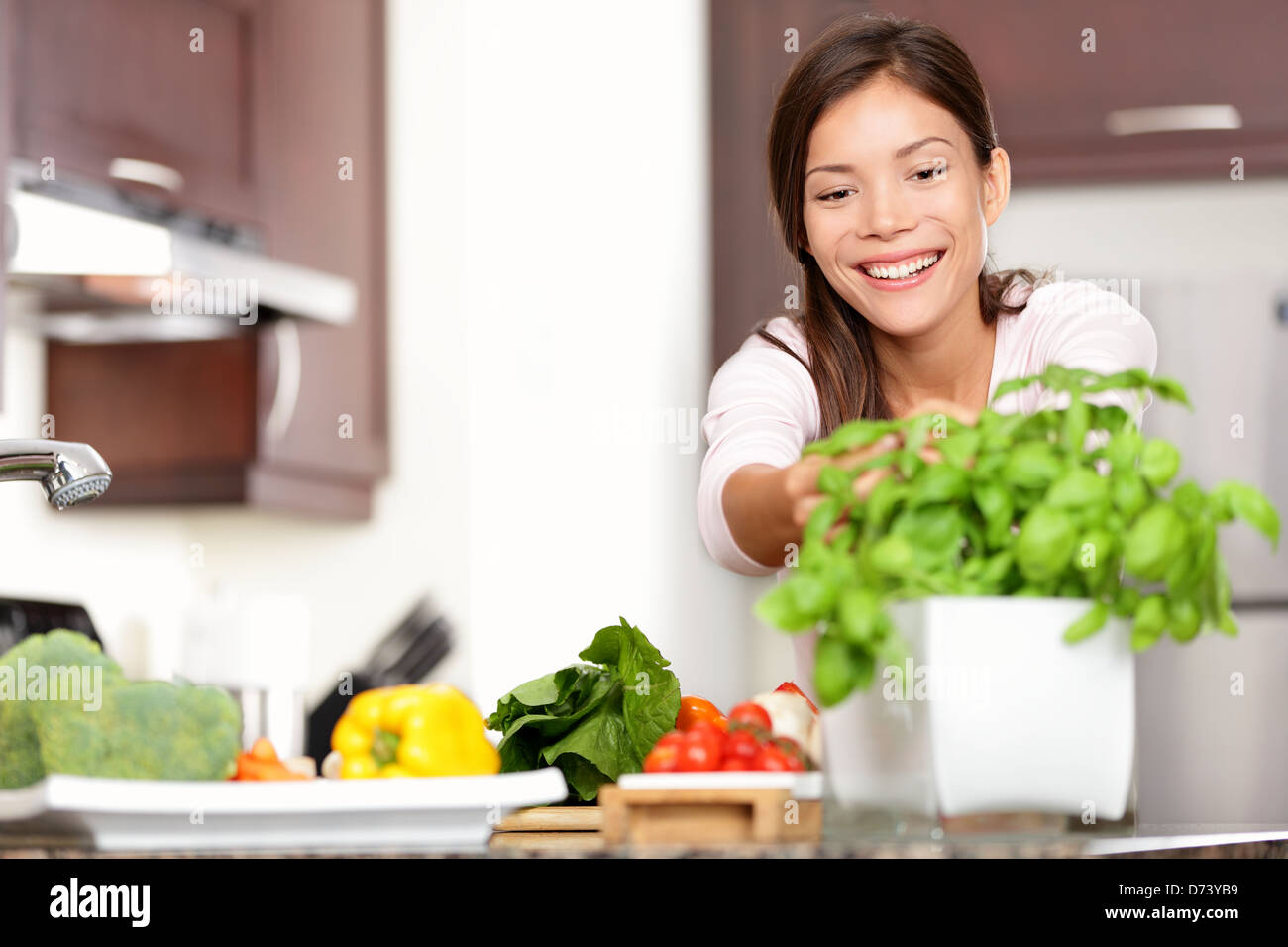 Woman making food in kitchen reaching for basil plant. Healthy eating ...