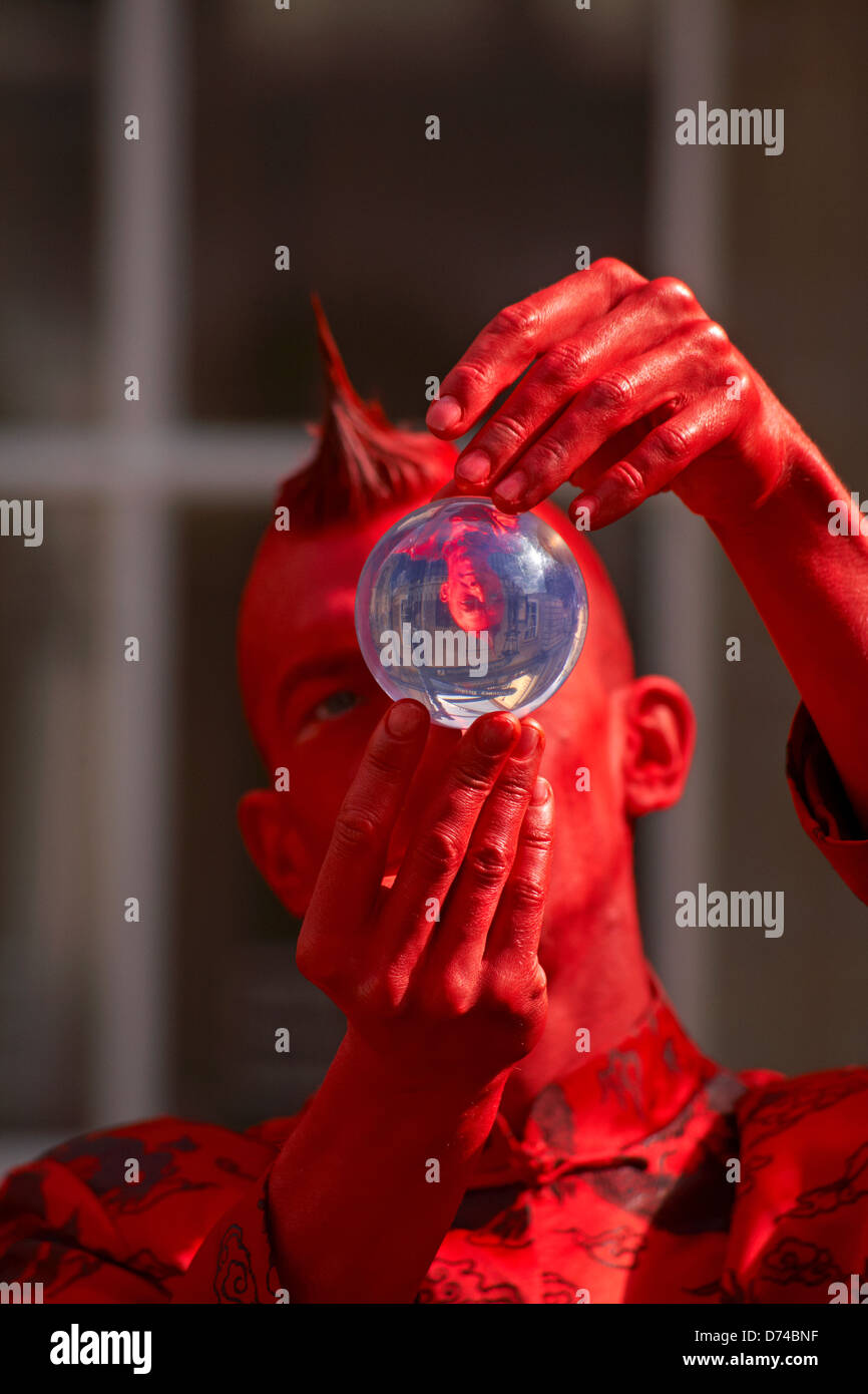 Street performer dressed in red with red face holding glass sphere ...