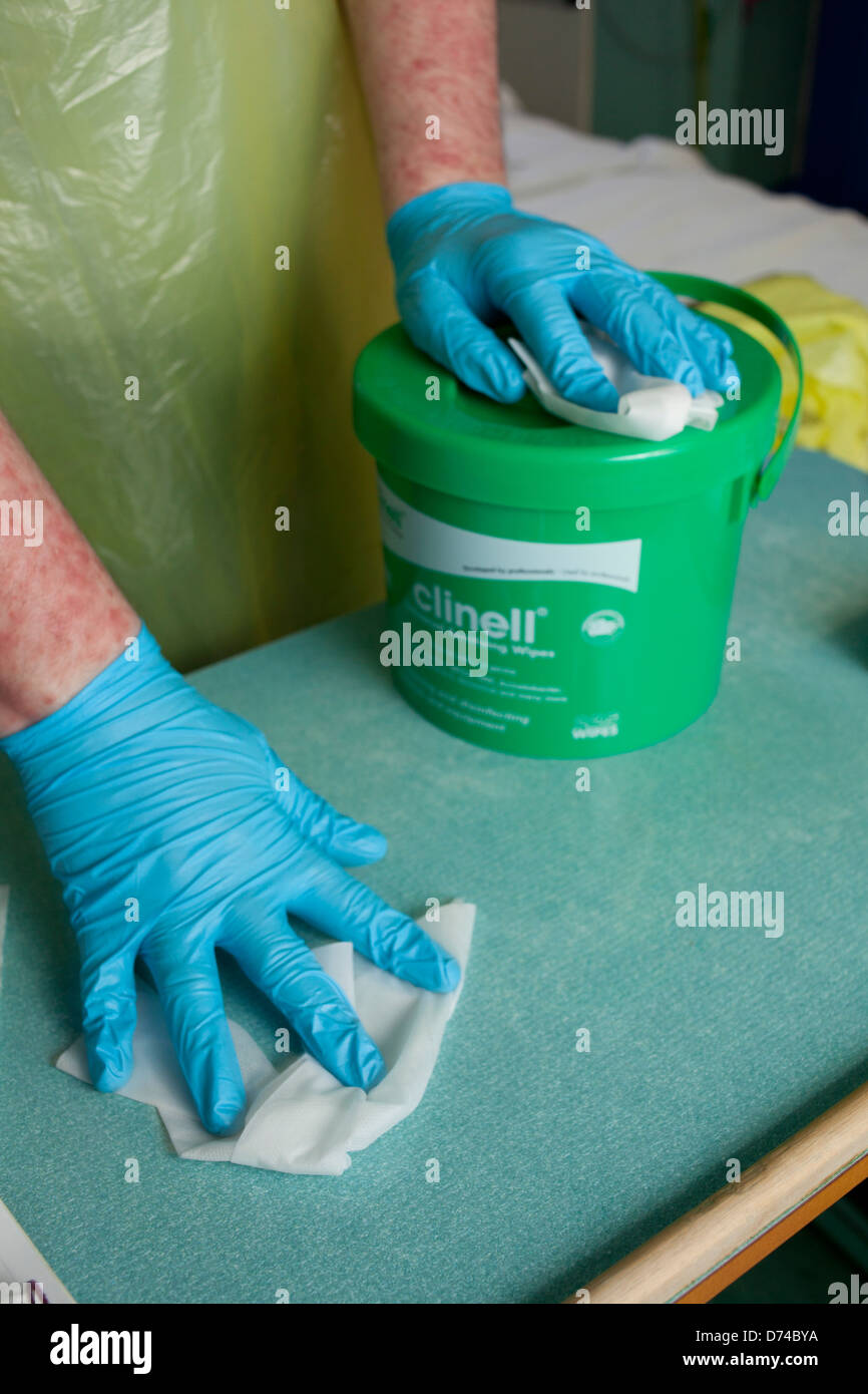 A hospital worker cleaning surfaces around a bed on a hospital ward ...
