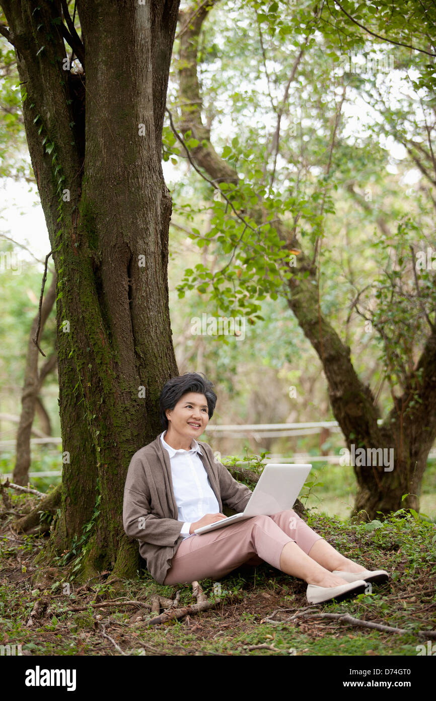 middle aged woman sitting under a tree using laptop Stock Photo - Alamy