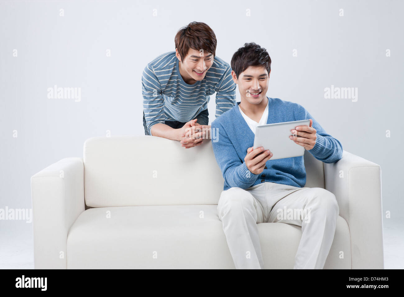 a man sitting on couch sharing tablet PC with man standing behind a ...