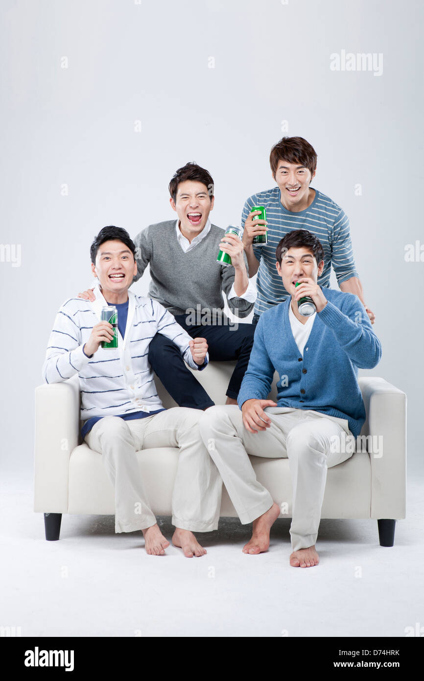 four men on and around a couch watching a TV drinking beer Stock Photo ...