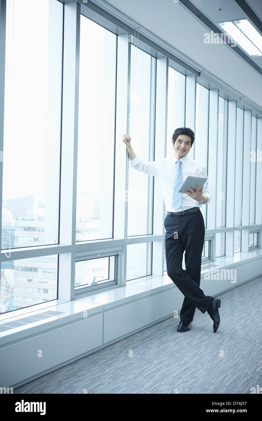 a businessman holding a tablet PC leaning on the window of an empty ...