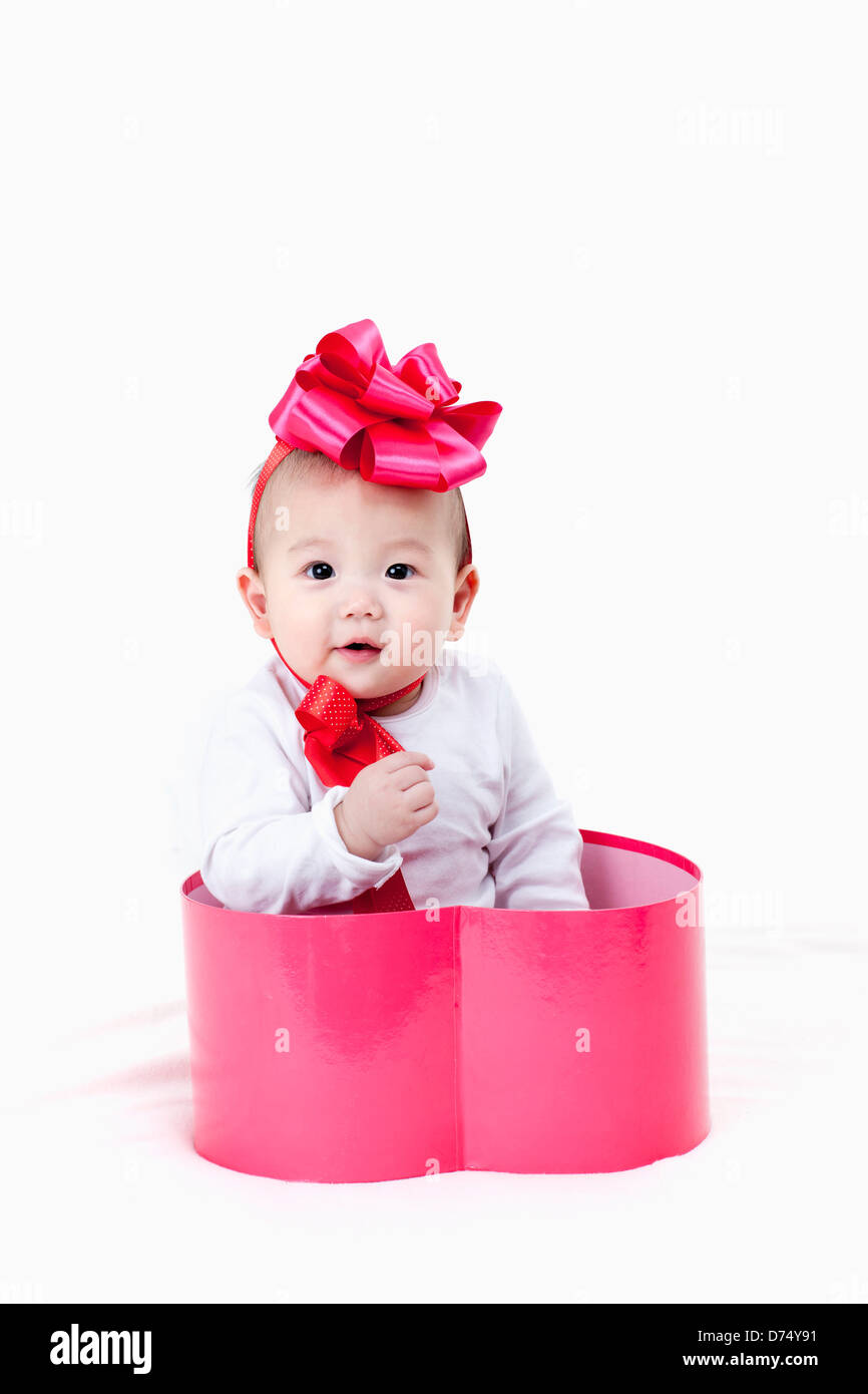 a baby inside a pink heart shaped gift box with a ribbon around head ...