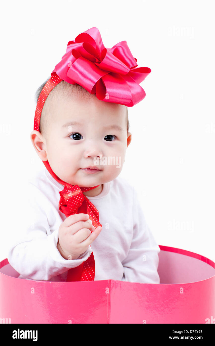 a baby inside a pink heart shaped gift box with a ribbon around head ...