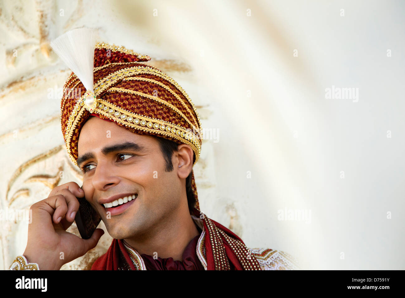 Indian groom in traditional wedding outfit and talking on a cell phone ...