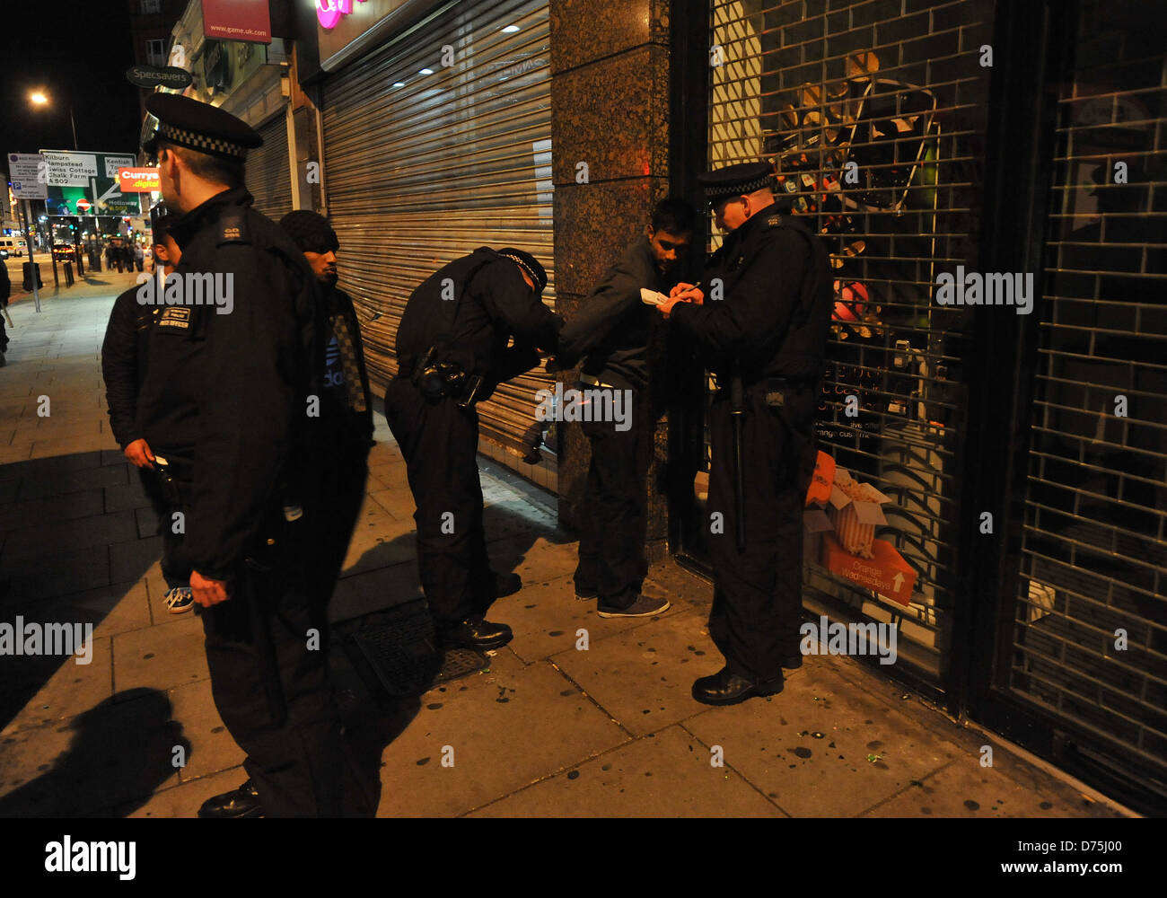 Police officers search a man as rioters attack shops and property ...
