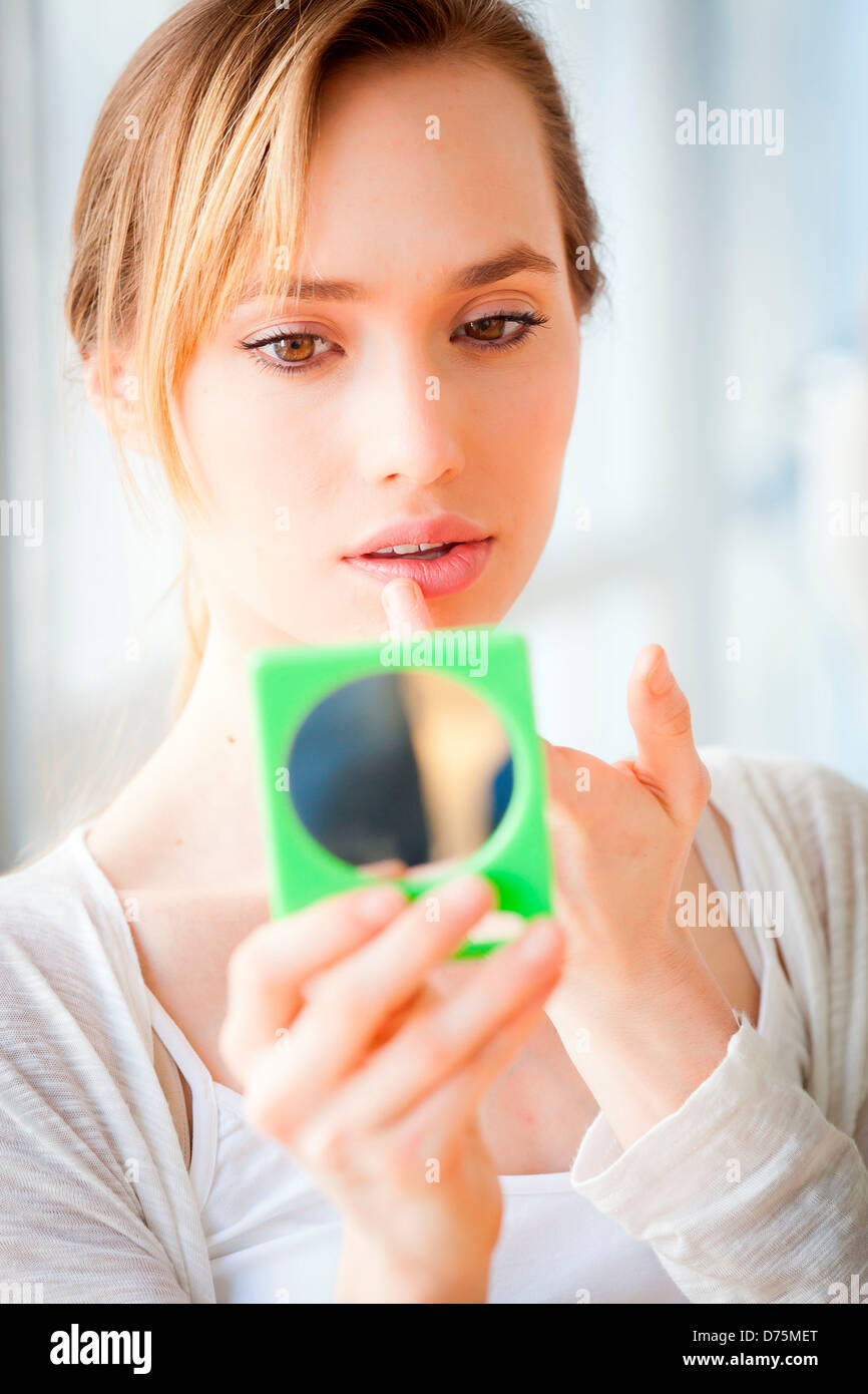 Young woman checking her face in the mirror Stock Photo - Alamy