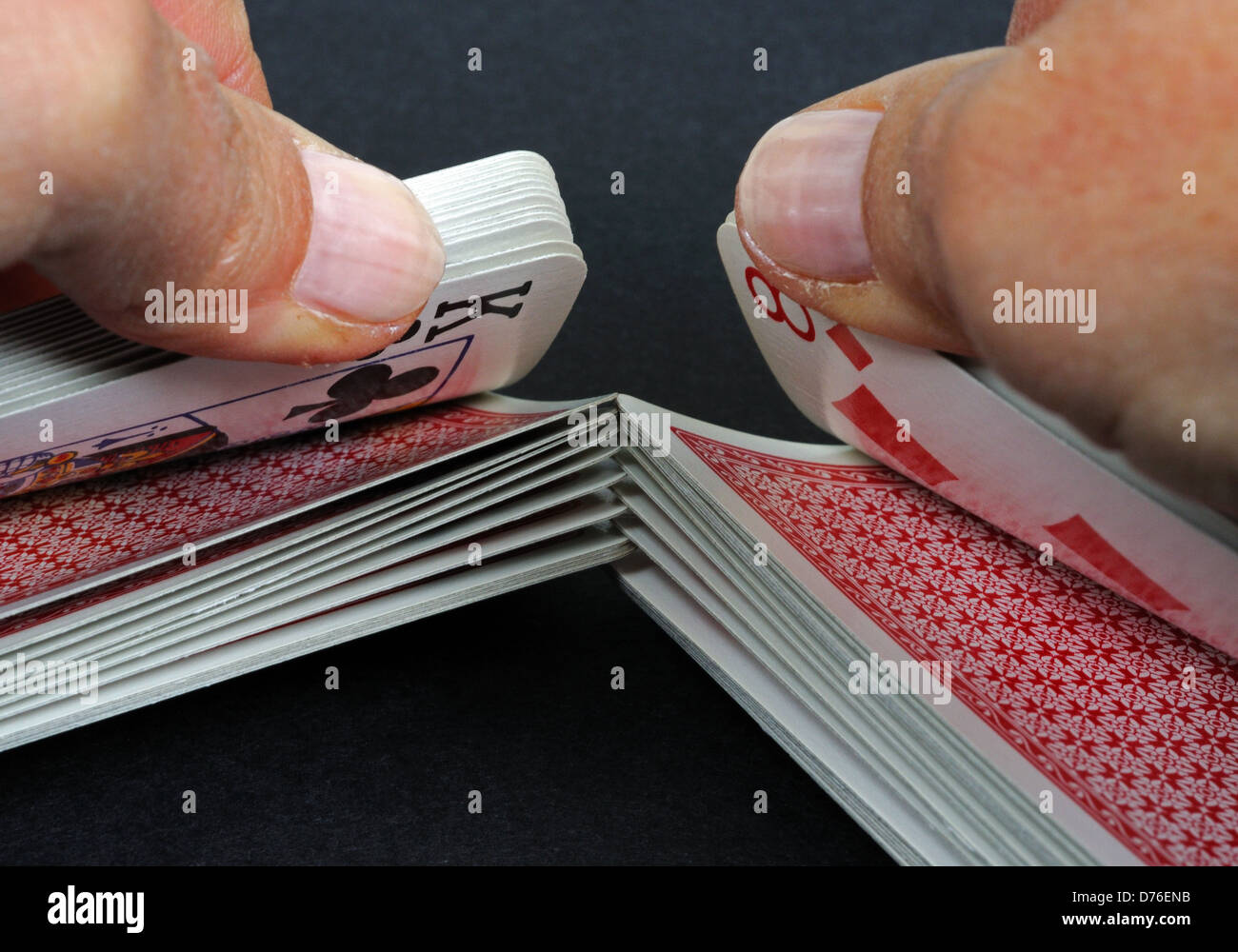 Woman shuffling a pack of playing cards against a black background ...