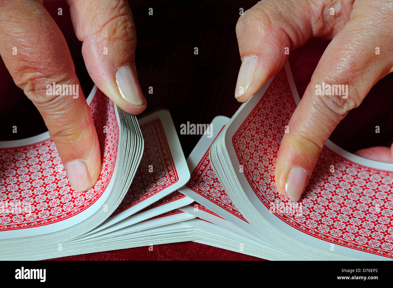Woman riffle shuffling a pack of playing cards against a black ...