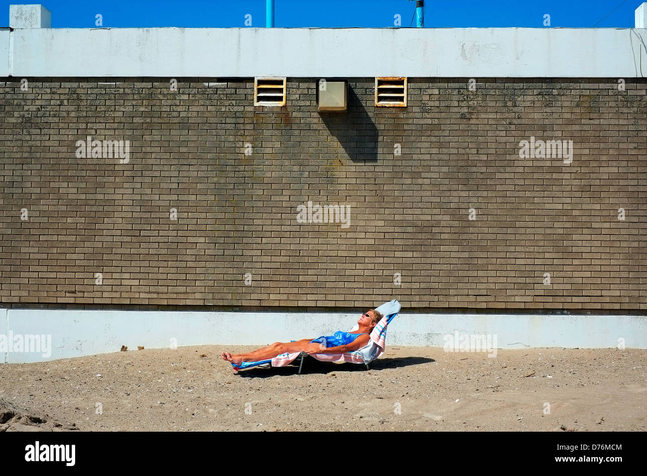 A woman lies sleeping on a sun lounger on the beach at Coney Island ...