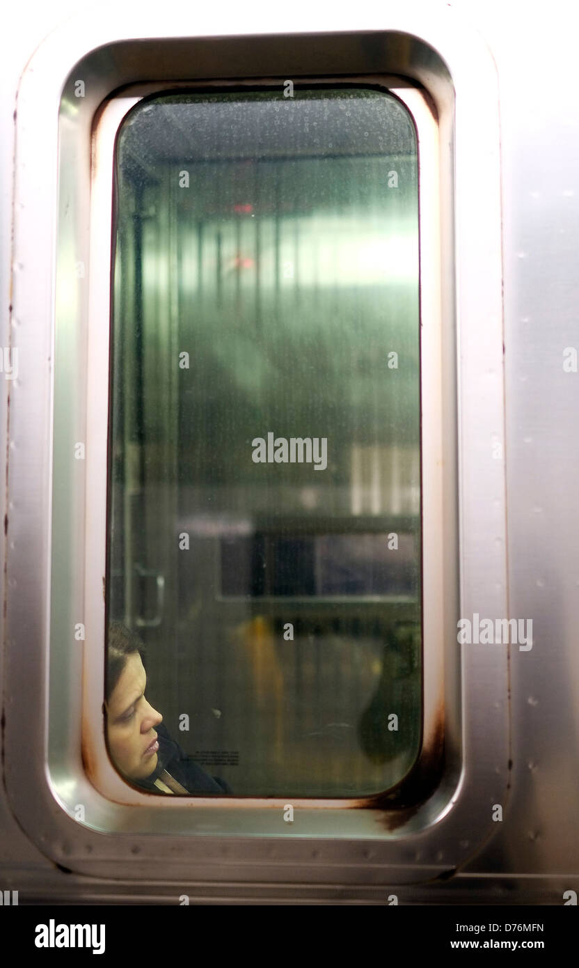 A commuter sleeps against the window of a New York City subway train ...