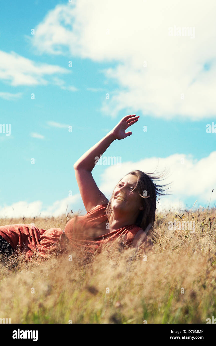 Happy young woman led down waving in a grassy field on a summers day ...