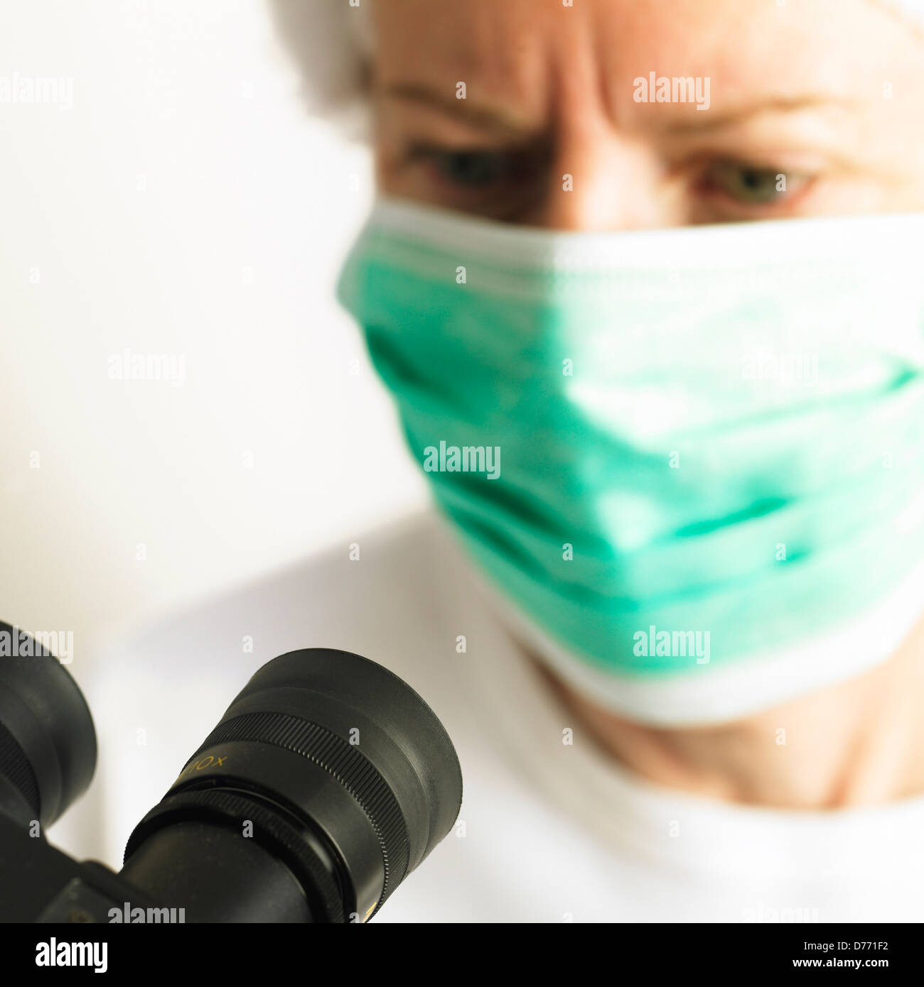 Female scientist wearing protective clothing looking through laboratory ...