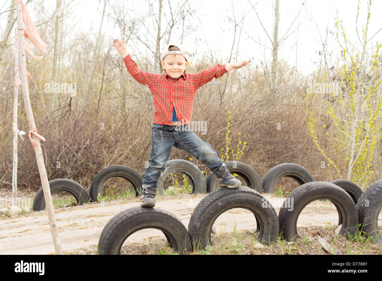 Cute little boy balanced on old tyres inserted into the ground on ...